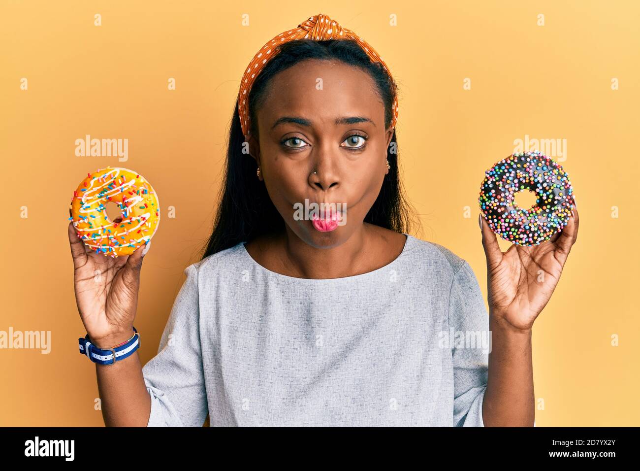 Young african woman holding tasty colorful doughnuts making fish face ...