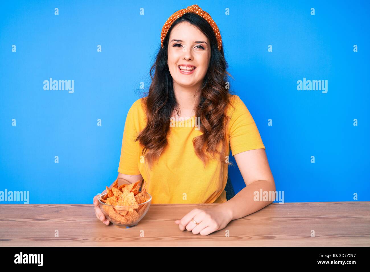 Young beautiful brunette woman sitting on the table eating nachos ...