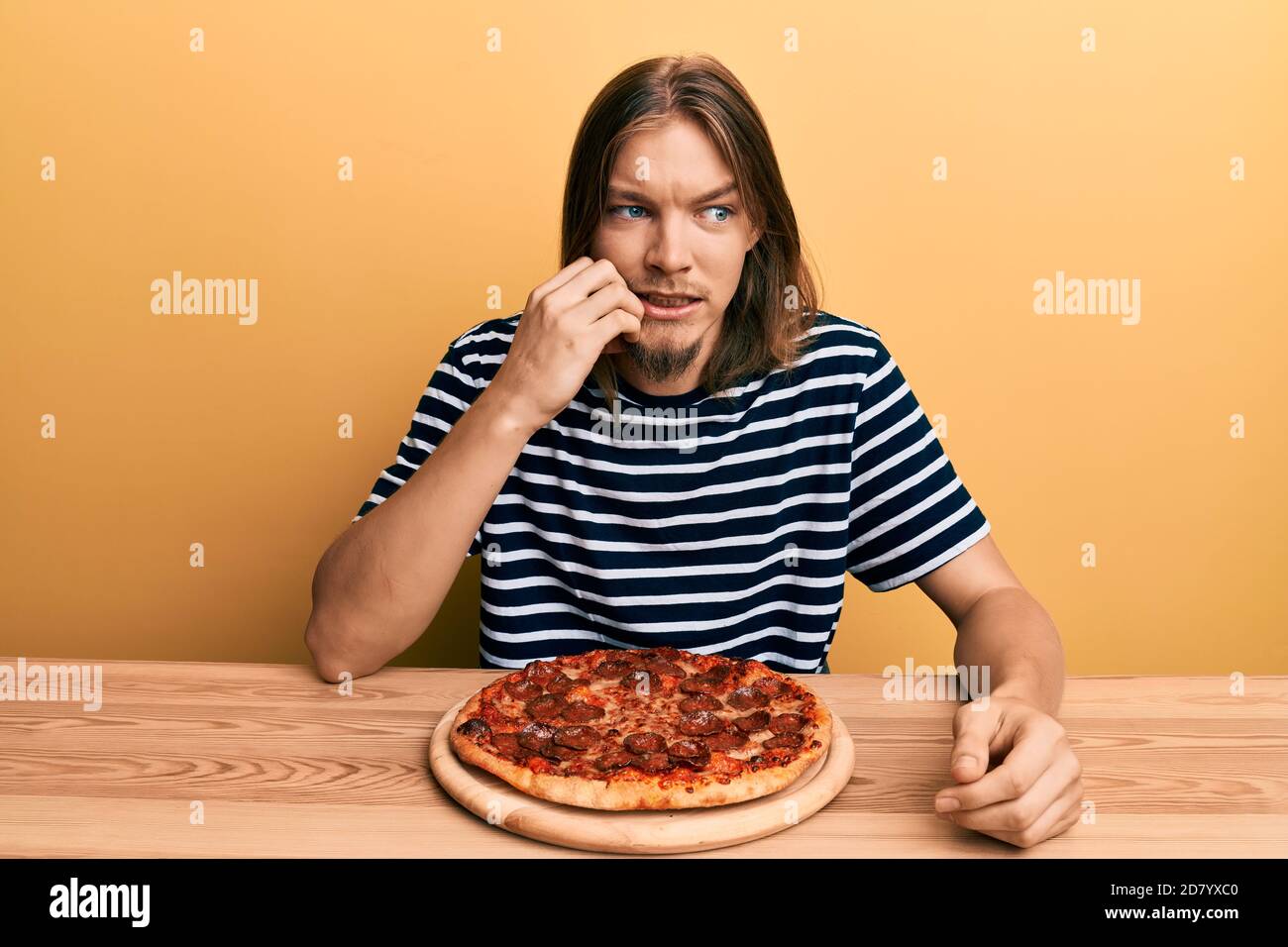 Handsome caucasian man with long hair eating tasty pepperoni pizza ...