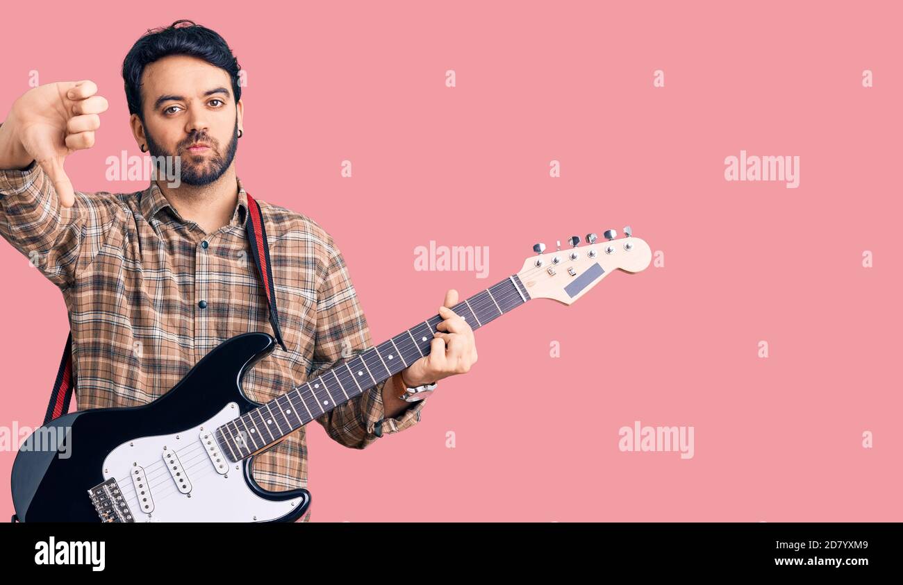 Young hispanic man playing electric guitar with angry face, negative ...