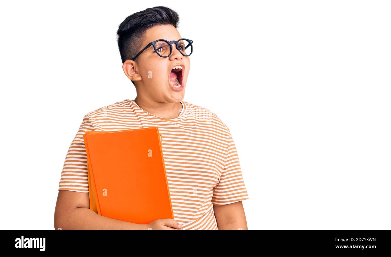 Little boy kid holding book wearing glasses angry and mad screaming ...