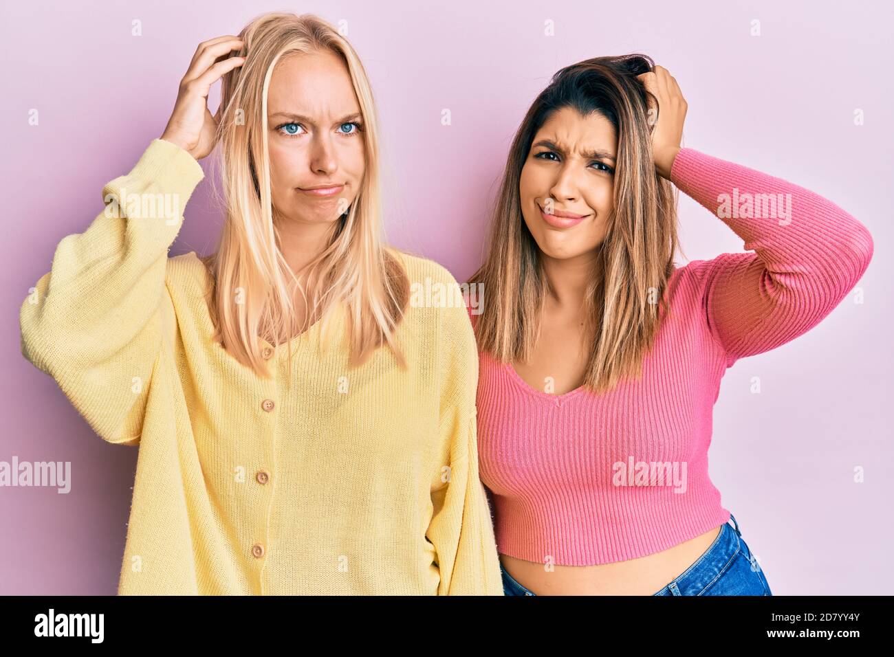 Two friends standing together over pink background confuse and wonder ...