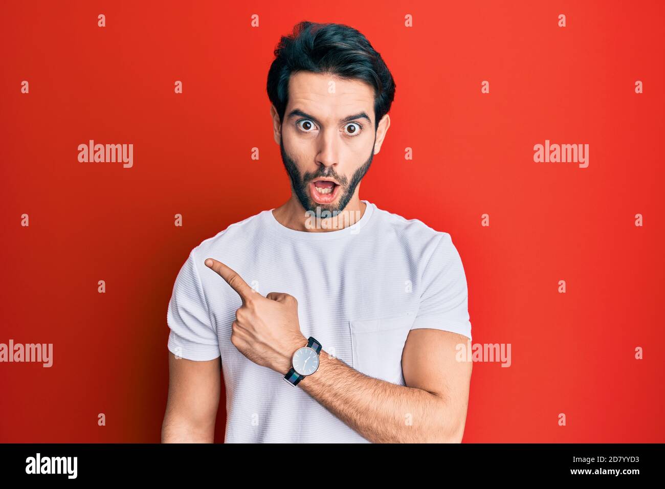 Young hispanic man wearing casual white tshirt surprised pointing with ...