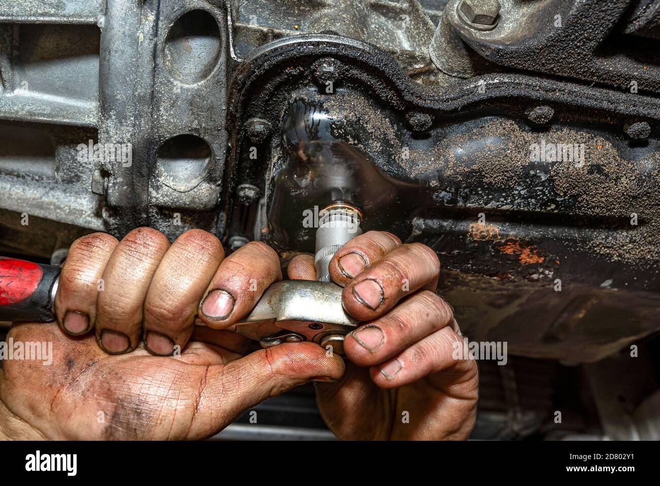 The car mechanic bolts a new screw with a copper washer to the oil sump ...