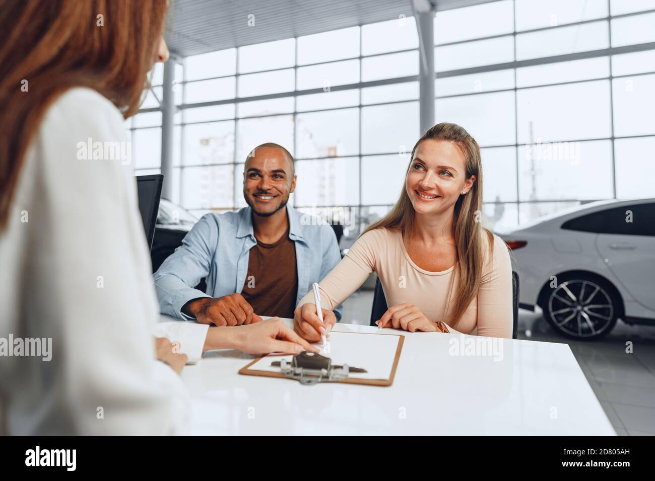 Beautiful young couple signs documents at car dealership showroom Stock ...