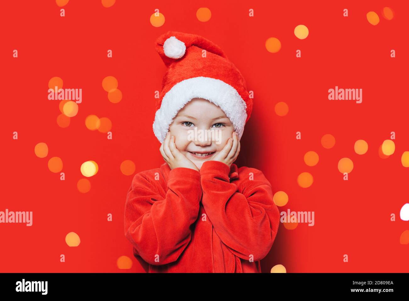 A little boy in a red Christmas costume, a red Christmas hat on his ...