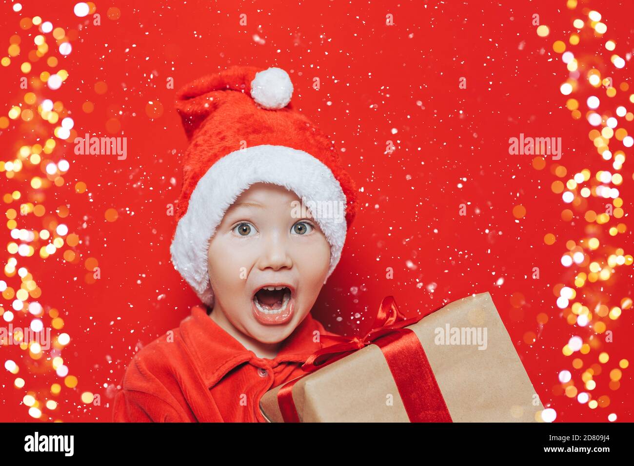 A little boy in a red Christmas costume, a red Christmas hat on his ...