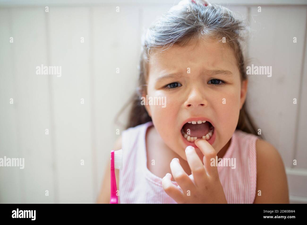 Front view portrait of worried small girl indoors, loosing baby tooth ...
