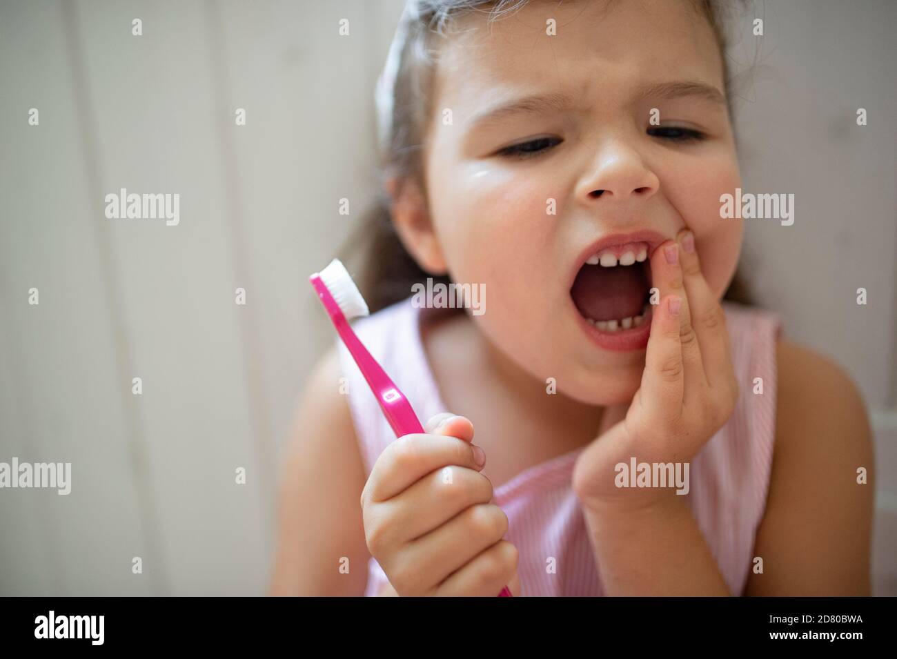 Front view portrait of worried small girl indoors, loosing baby tooth ...