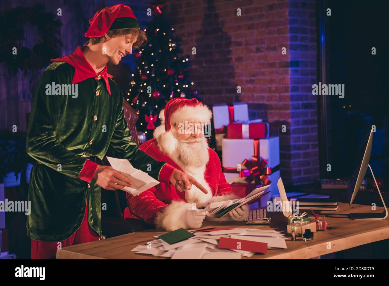 Photo portrait of elf pointing finger at letters in santa claus' hands ...