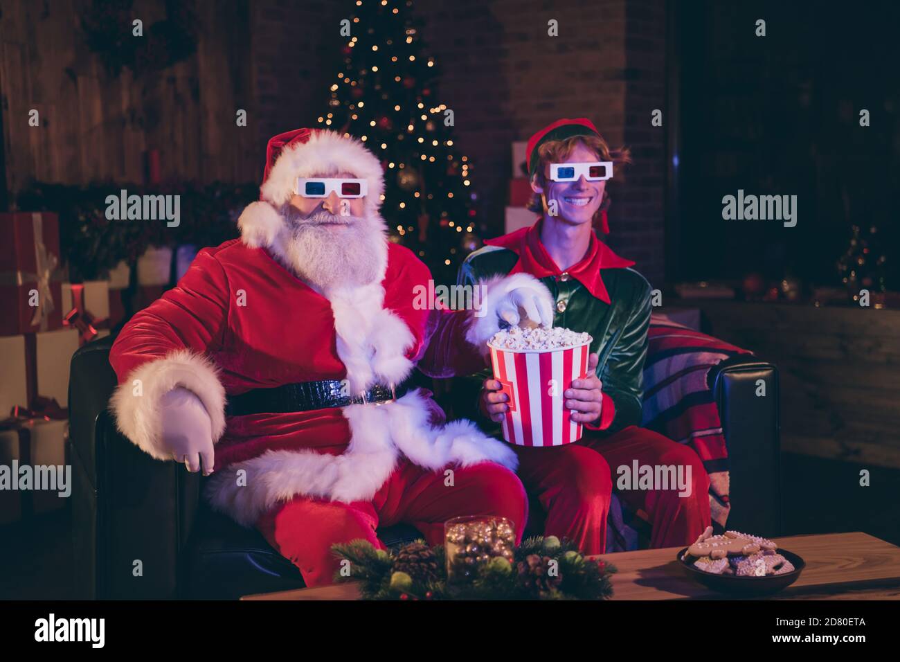 Photo portrait of santa claus and elf eating popcorn watching movie on ...