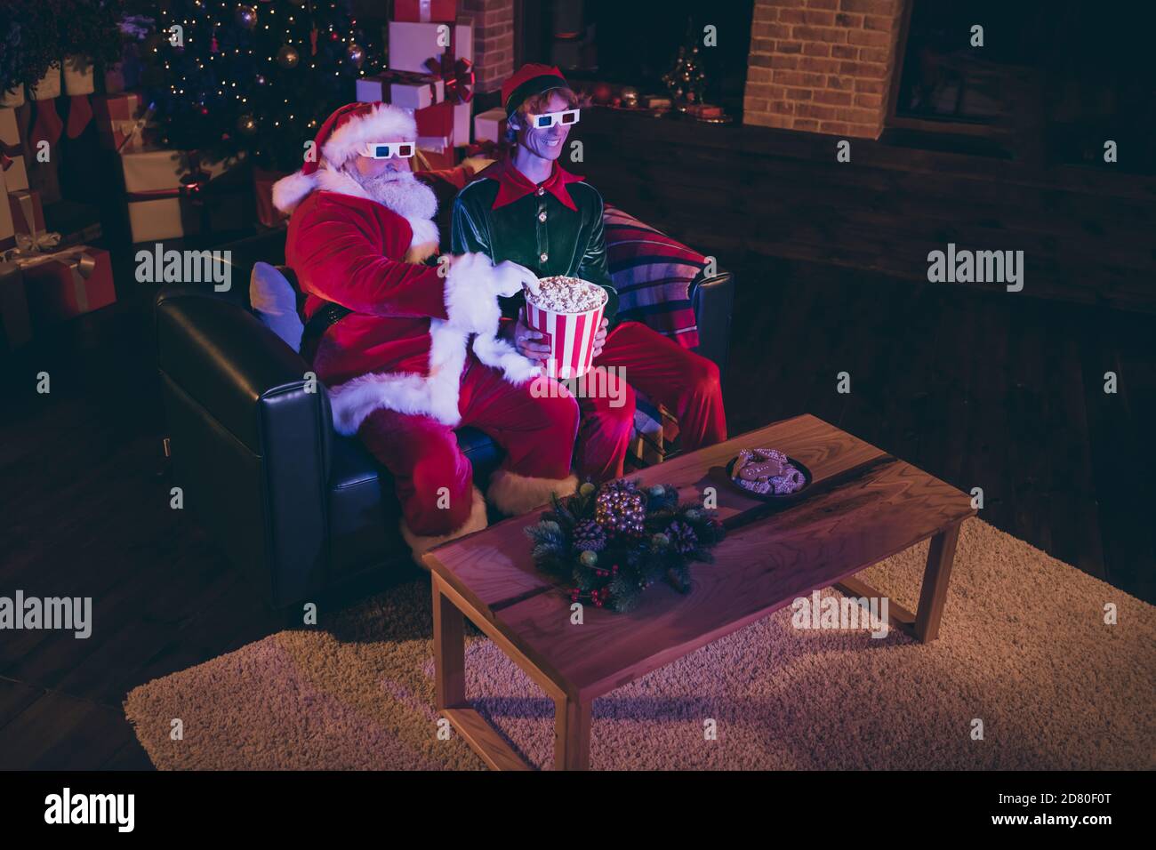 Photo portrait of santa claus taking popcorn from elf's lap watching ...