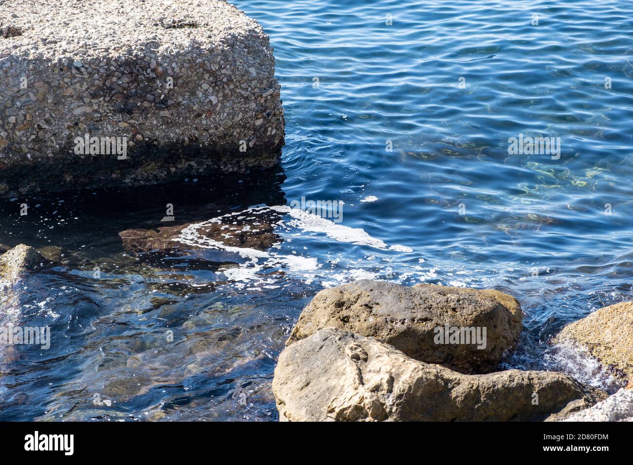 Sea pollution concept. Foam between rocks on the sunny water surface ...