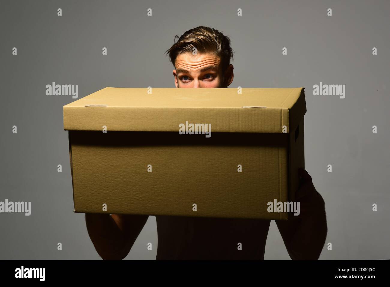 Macho with surprised eyes hides behind box. Guy holds box in front of ...