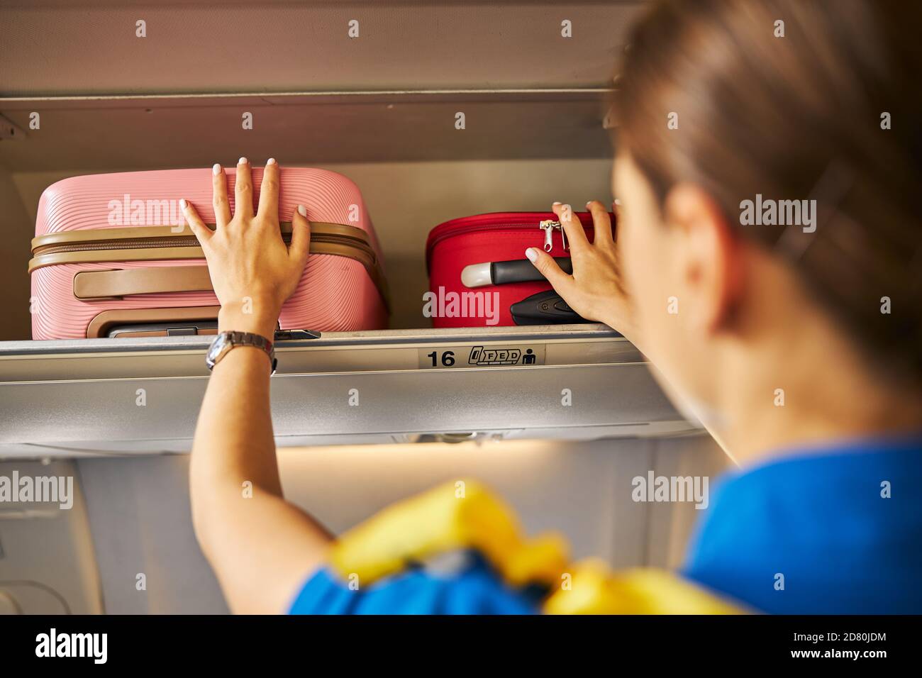 Air hostess fixating two bags on a shelf Stock Photo - Alamy