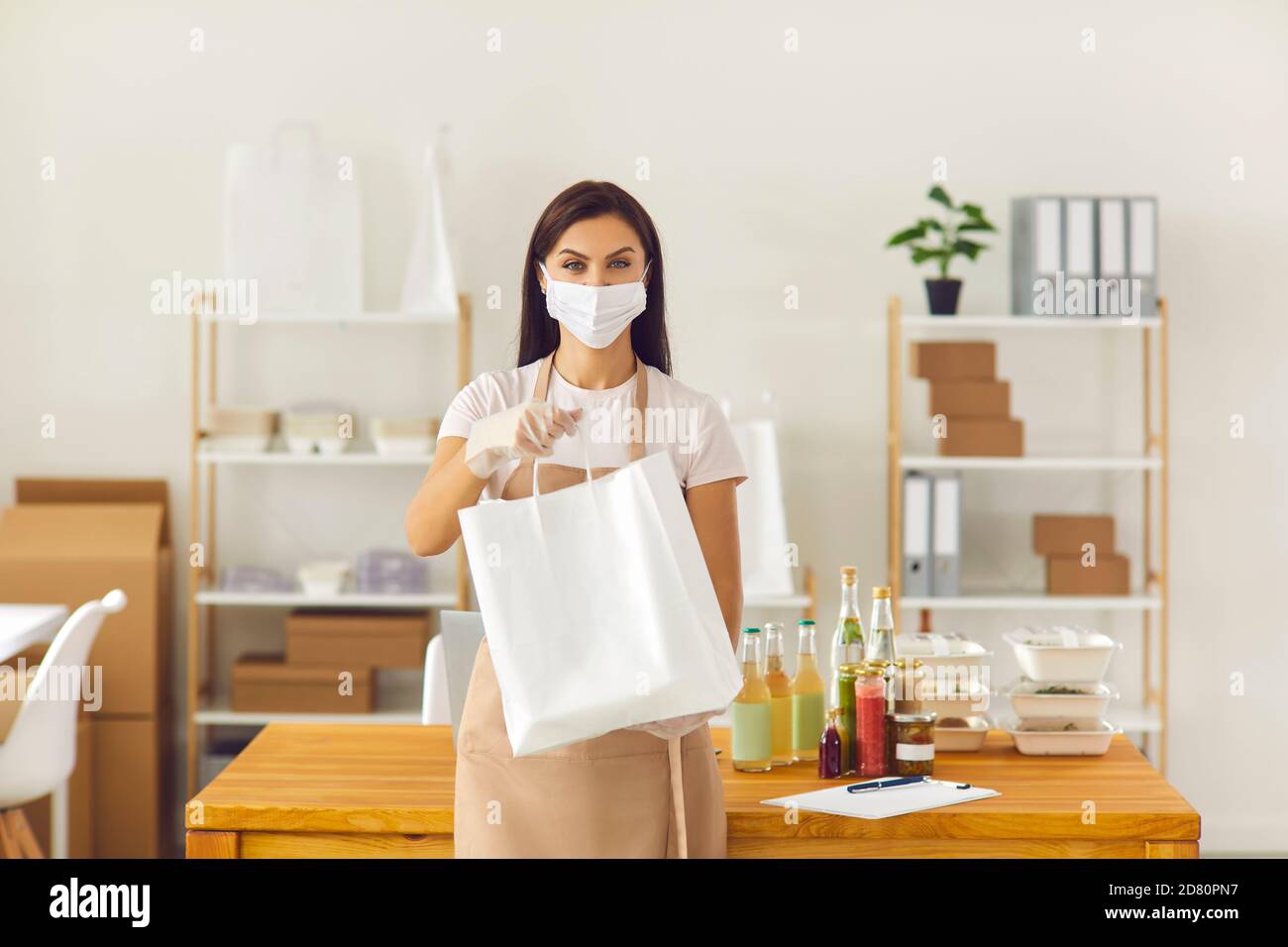 Cafe worker in medical face mask holding bag with fresh lunch ready for ...