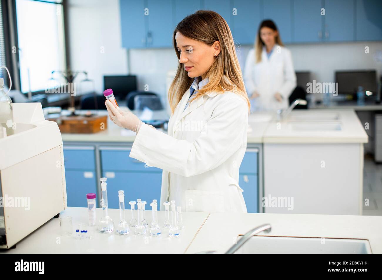 Young female doctor wearing protective face mask in lab holding flask ...