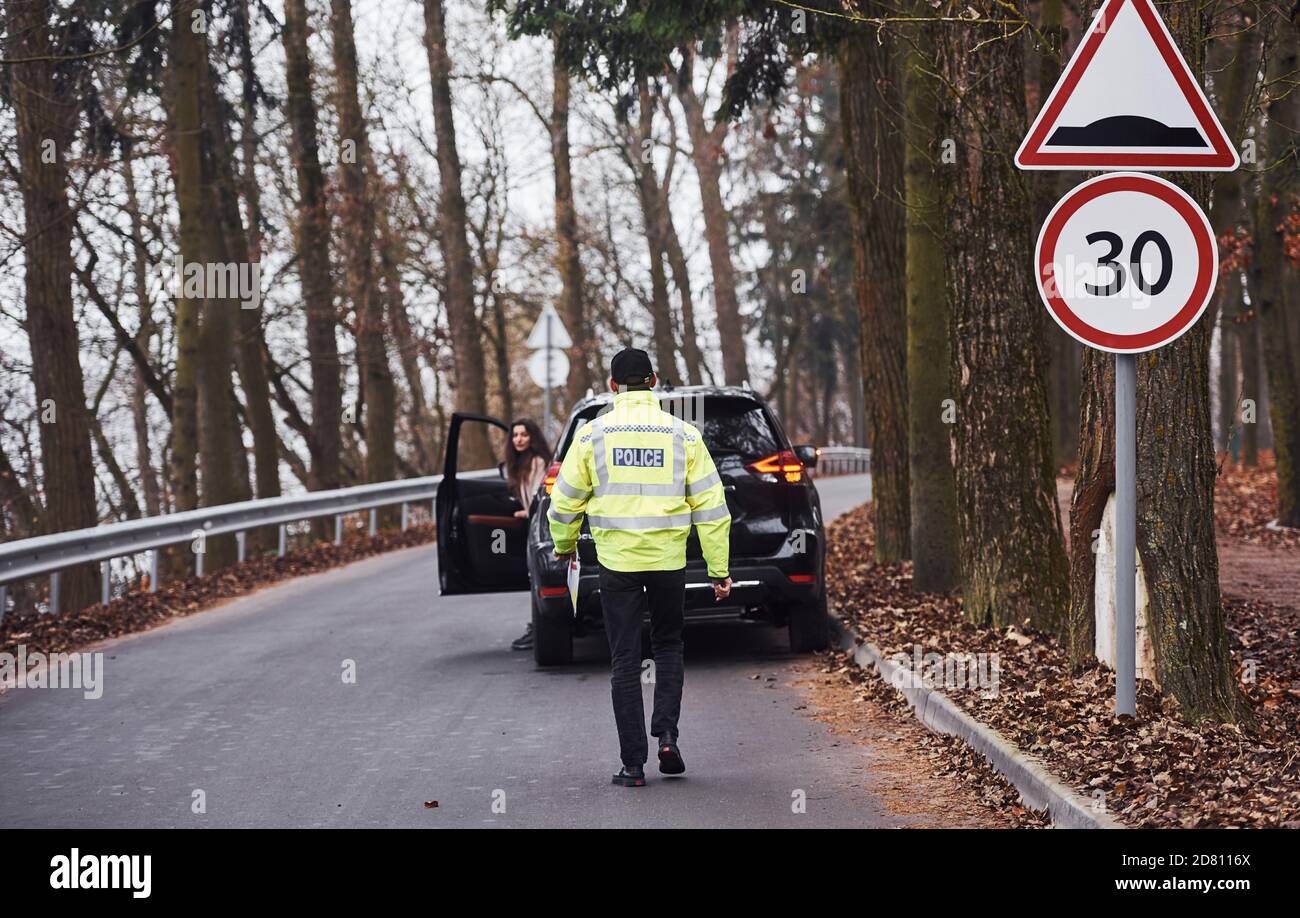 Male police officer in green uniform walking to the vehicle on the road ...
