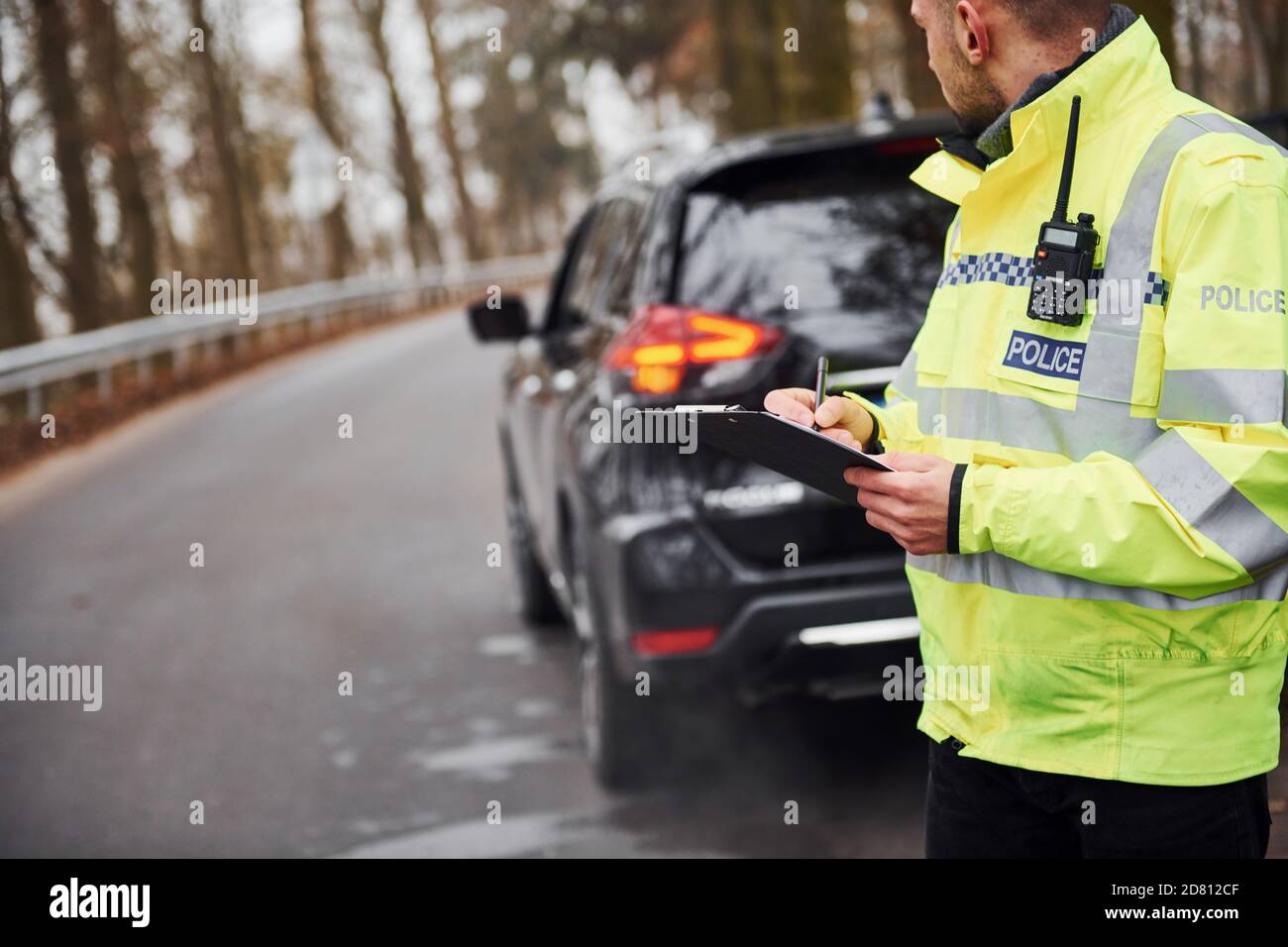 Male police officer in green uniform standing with notepad near car ...