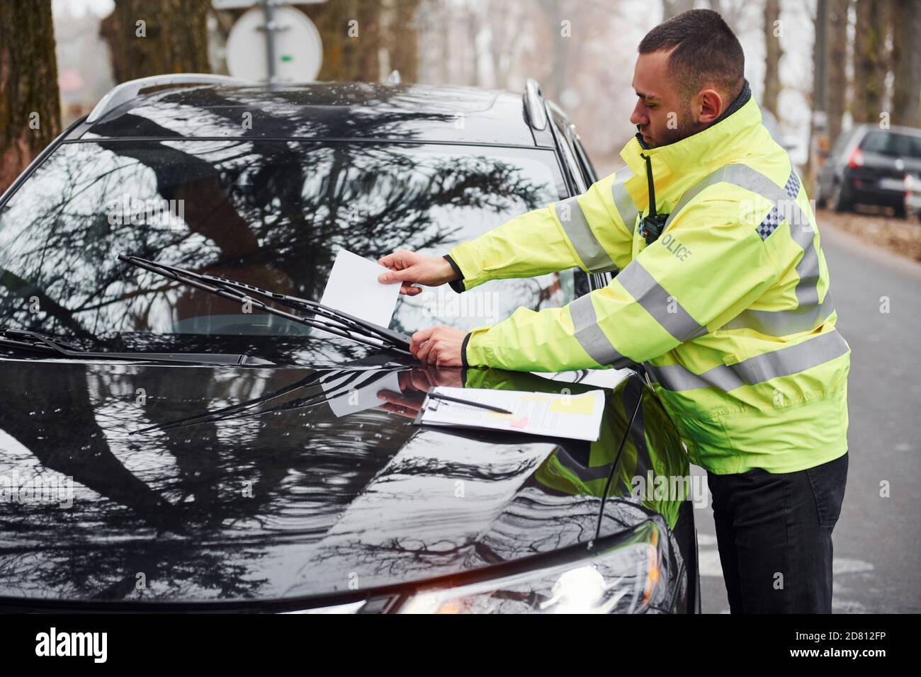 Male police officer in green uniform putting fine list to the vehicle ...