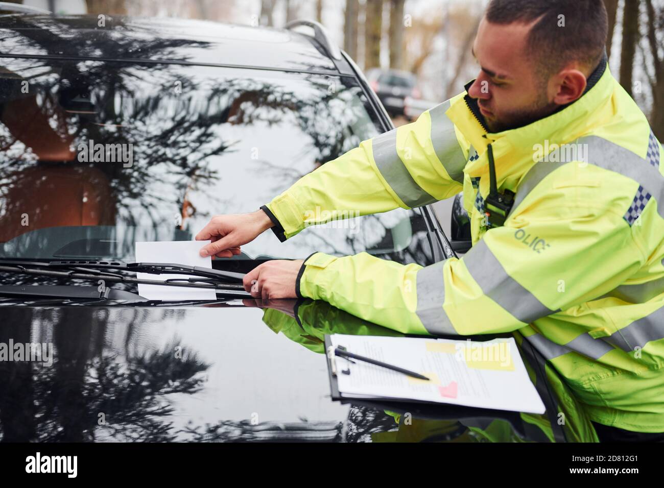 Male police officer in green uniform putting fine list to the vehicle ...