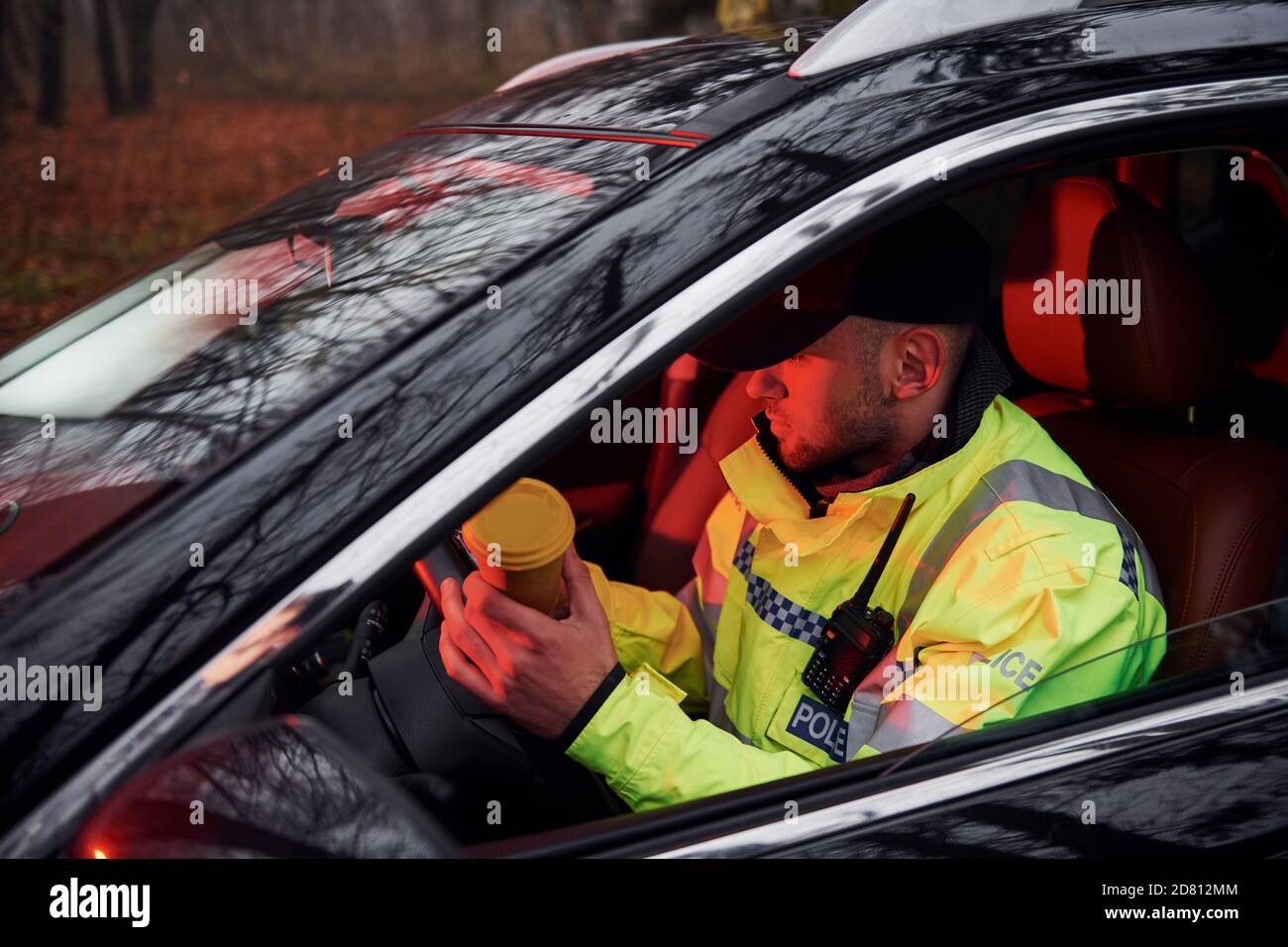 Male police officer in green uniform sitting in automobile with cup of ...