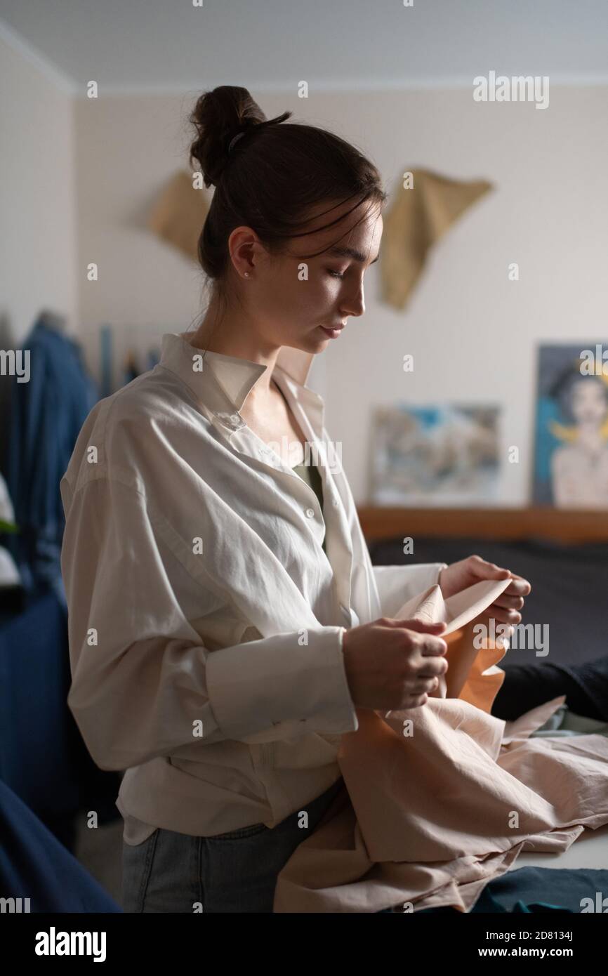 Side view of young female designer in white blouse and picking fabrics ...