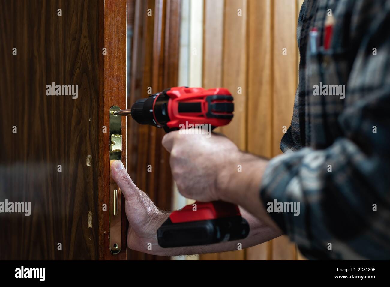 Close-up. Carpenter with an electric screwdriver fixes the lock of a ...