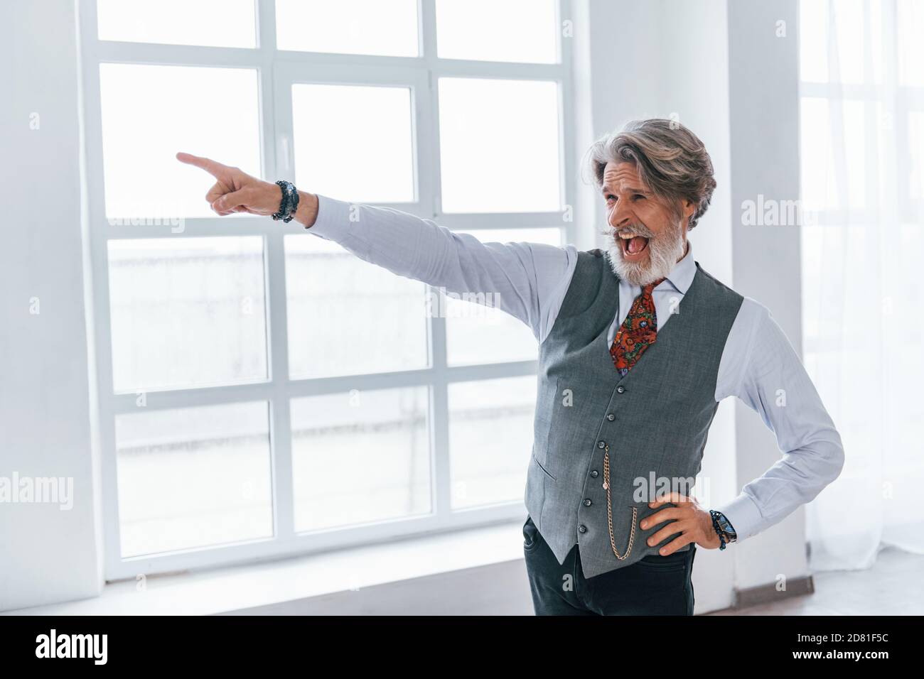 Screaming senior man in jacket and tie indoors in room against window ...