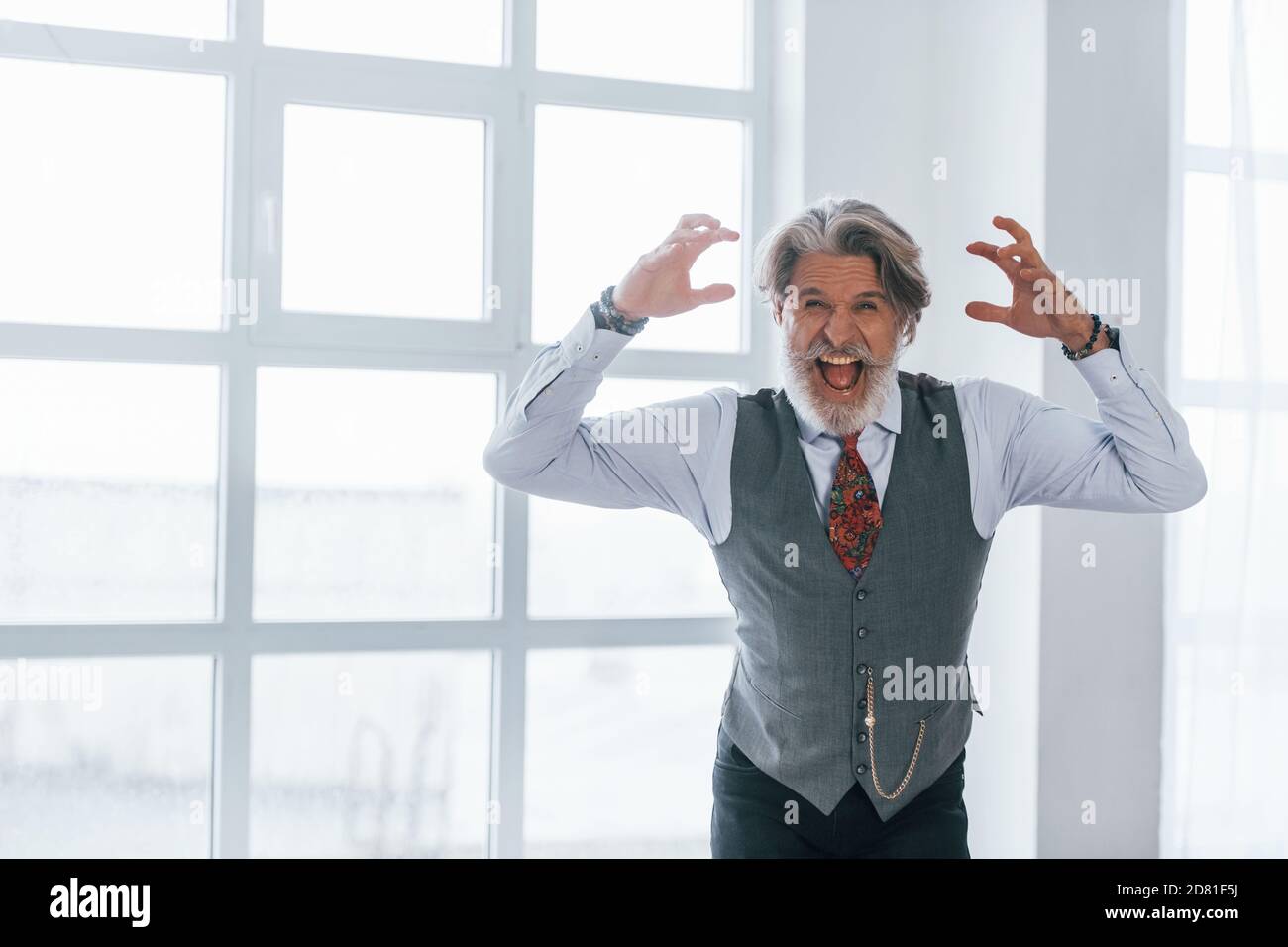 Screaming senior man in jacket and tie indoors in room against window ...