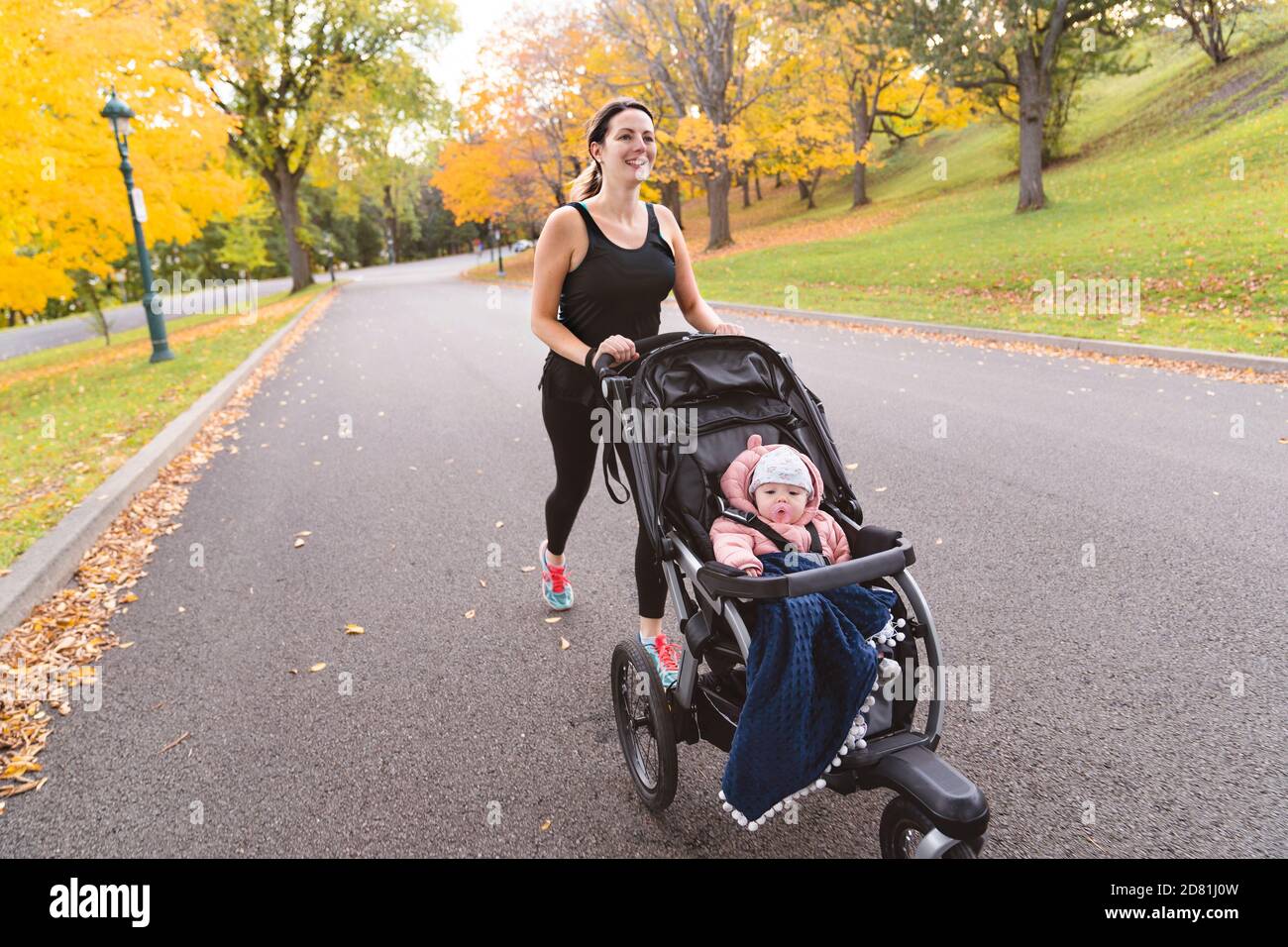 Beautiful young mother with her daughter in jogging stroller running ...