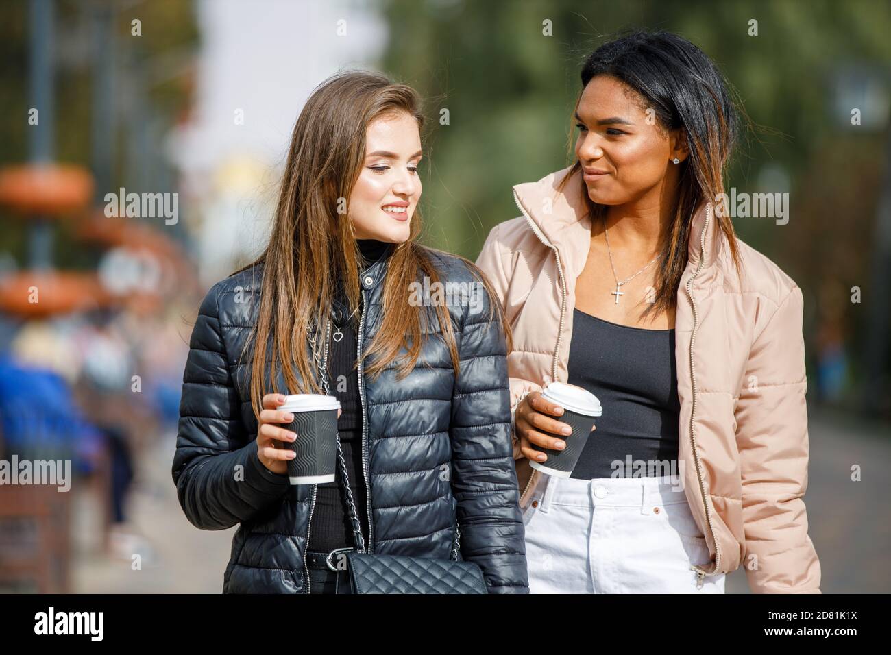 Two young women walking with coffee on the street Stock Photo - Alamy