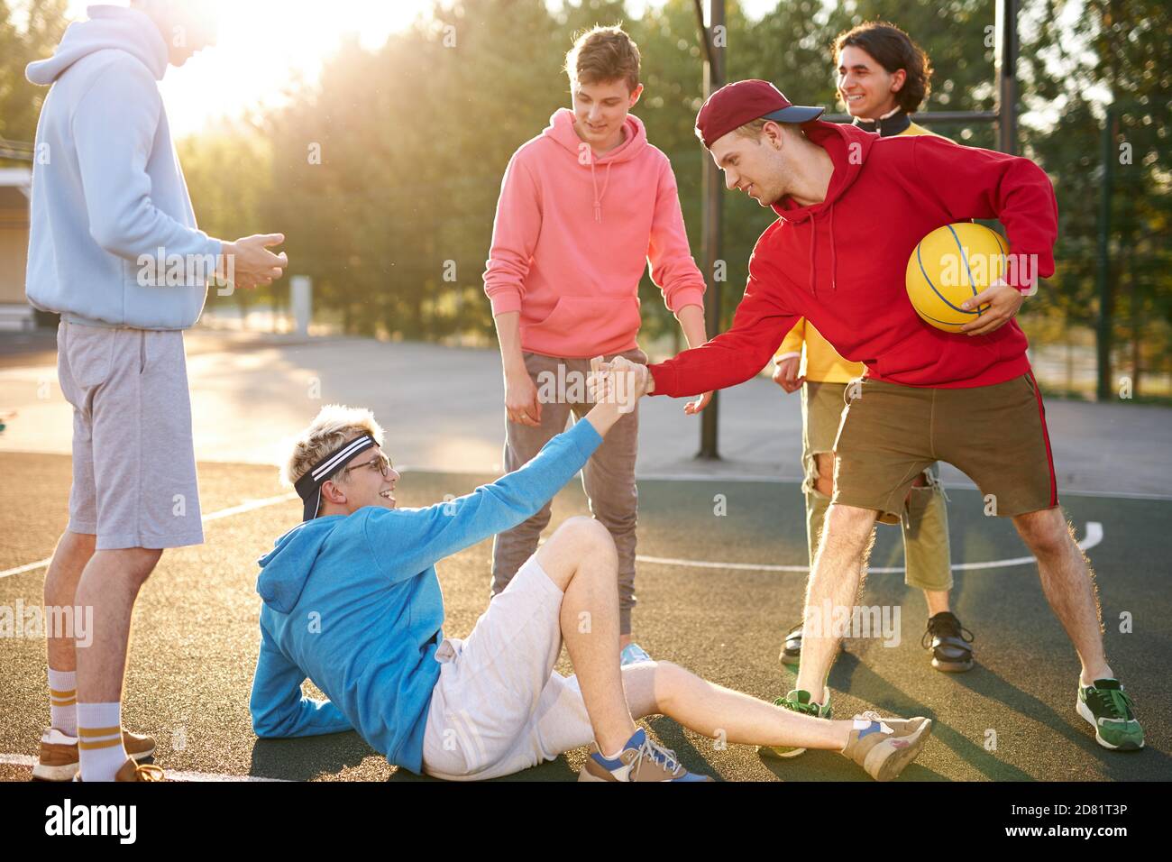 buddies reach out to a fallen friend at basketball court, caucasian ...