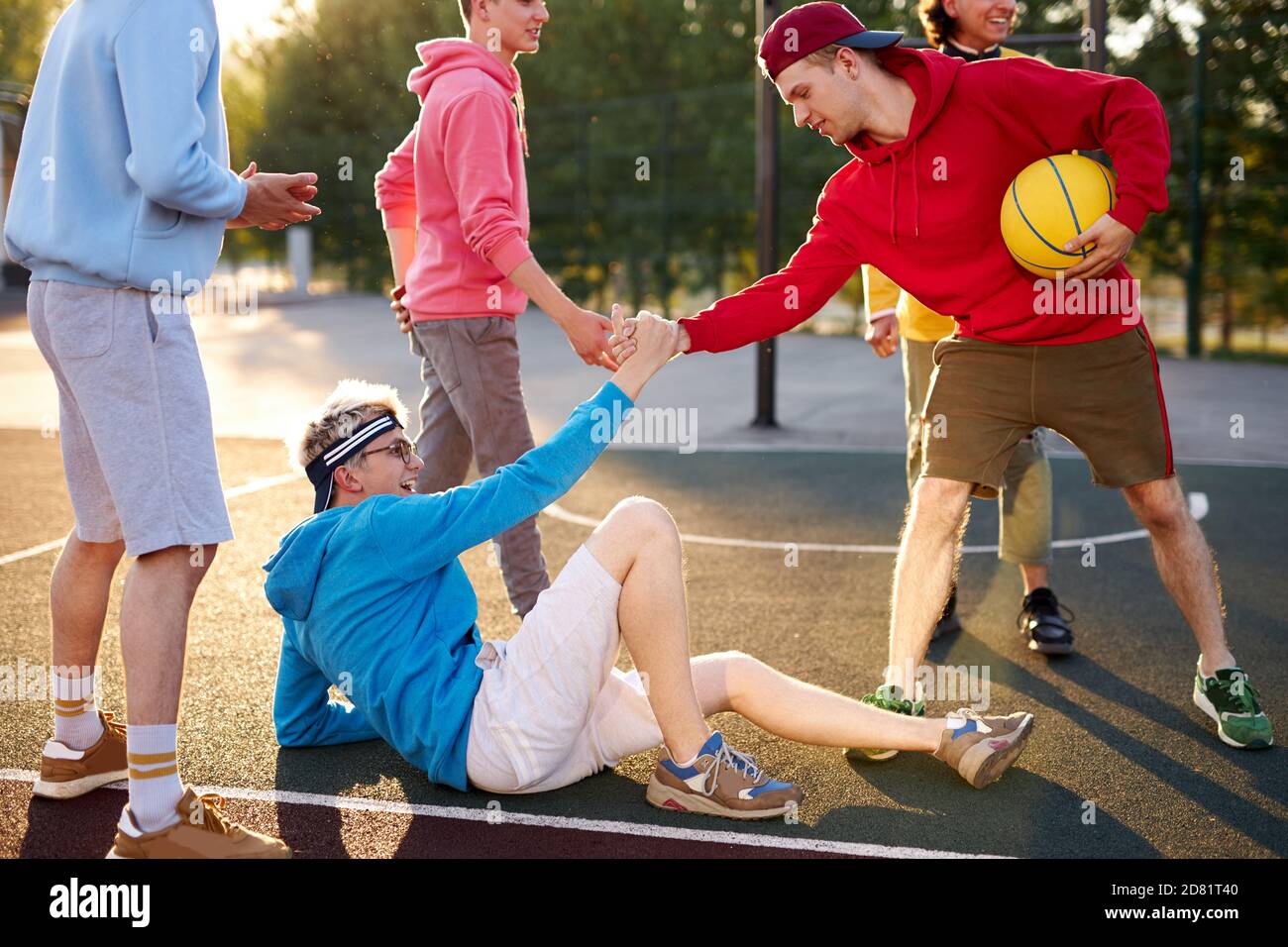 friend helps boy to get up after falling at basketball court, after ...