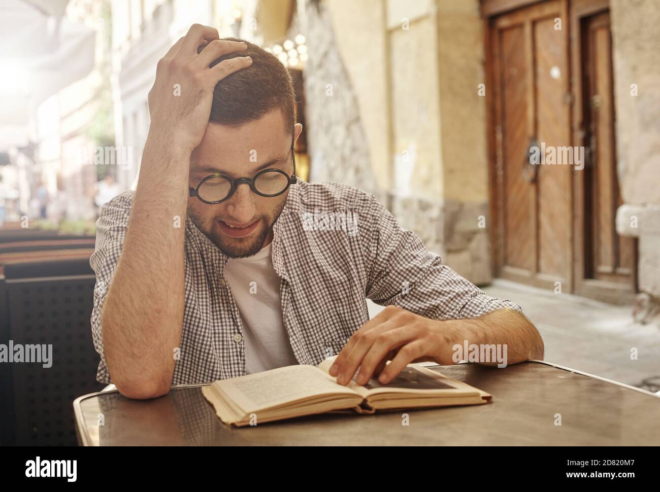 College student sitting and reading a book on the street in a cafe ...