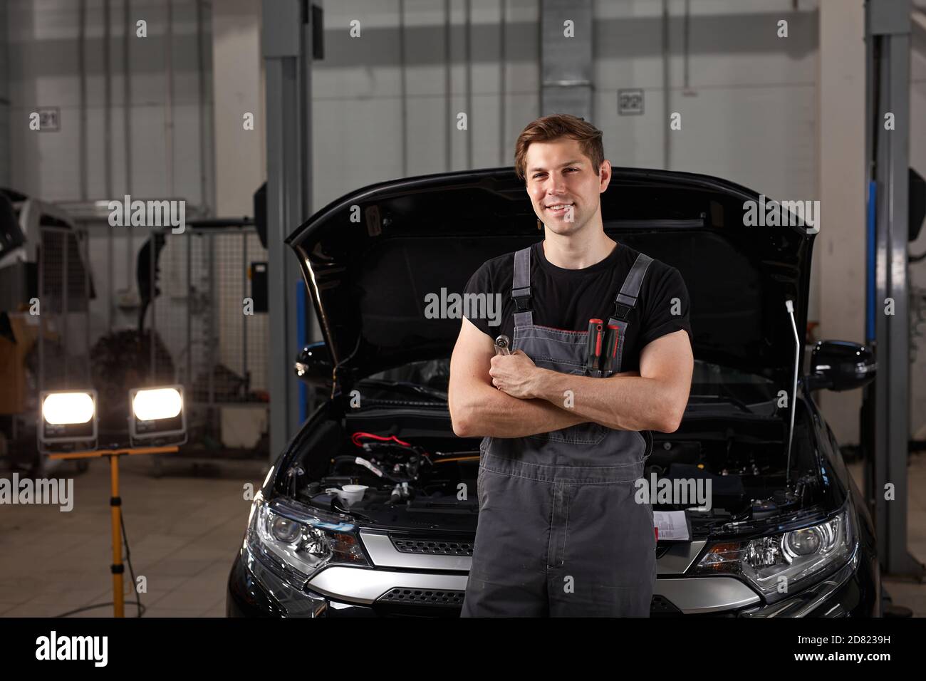 portrait of handsome caucasian auto mechanic man, standing near the car ...