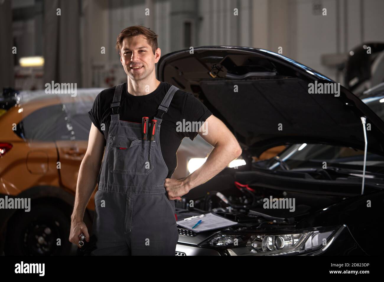 portrait of handsome caucasian auto mechanic man, standing near the car ...