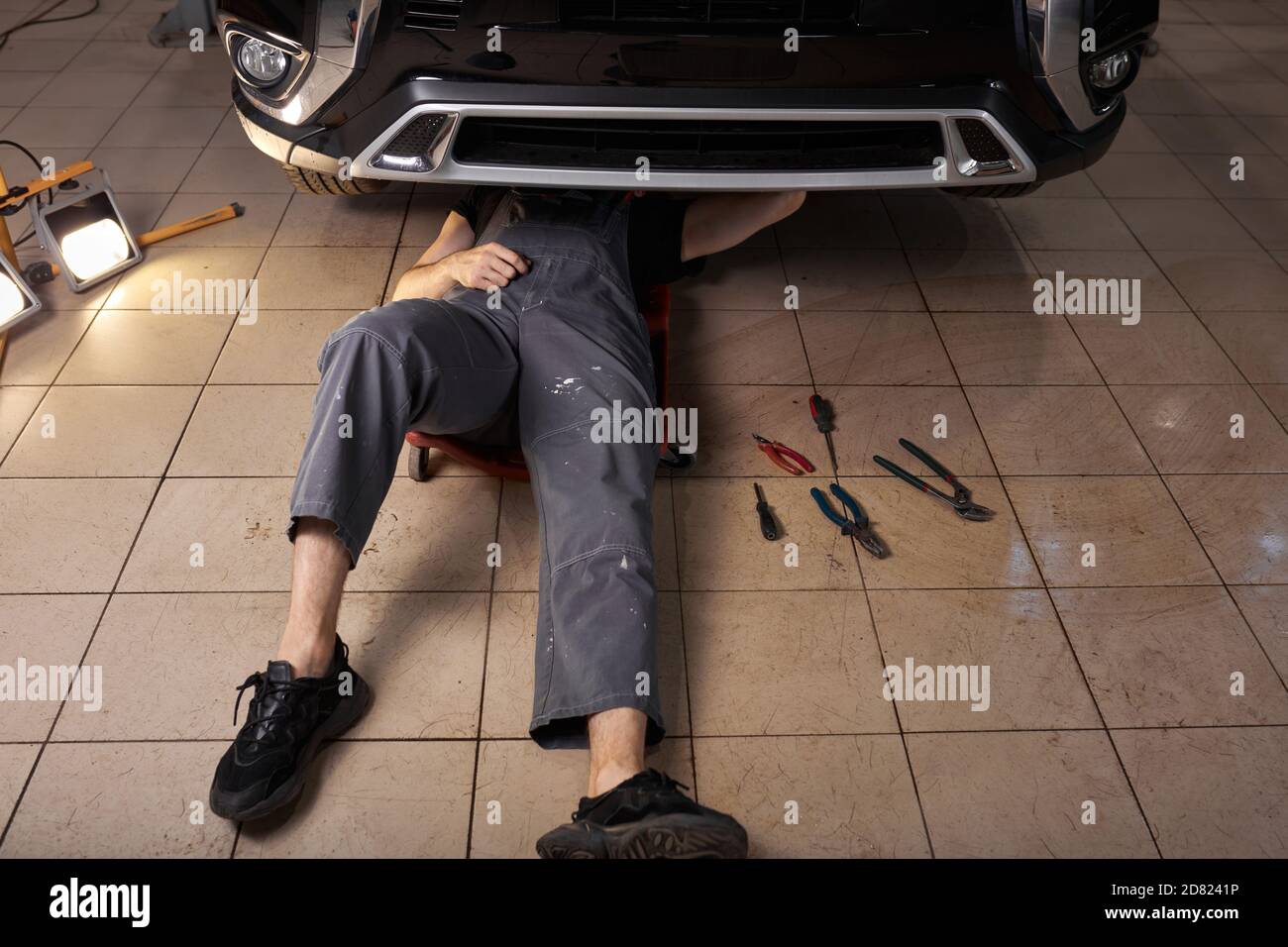 unrecognizable auto mechanic lying and working under car, top view ...