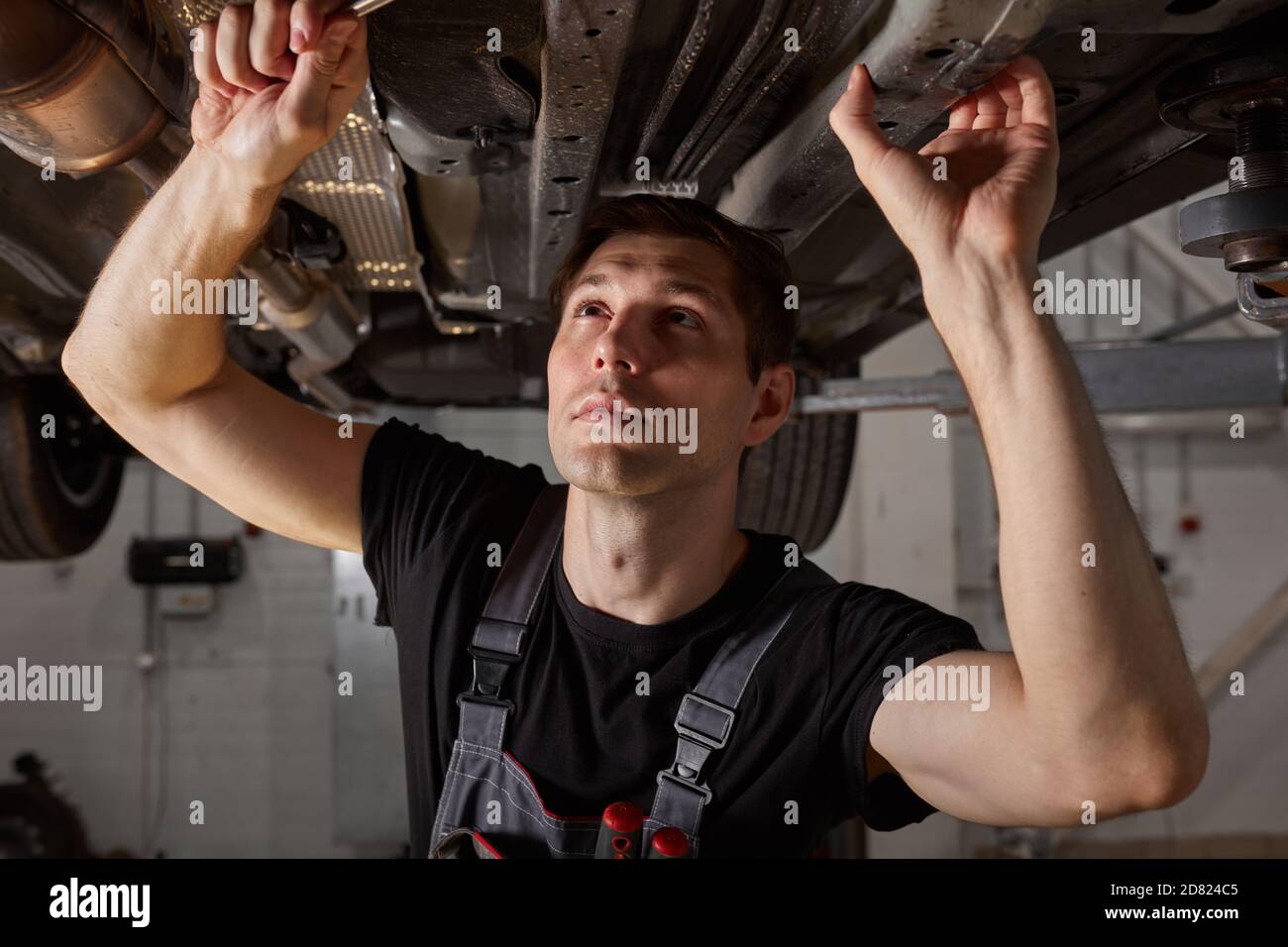 young male car mechanic in uniform checking car in automobile service ...