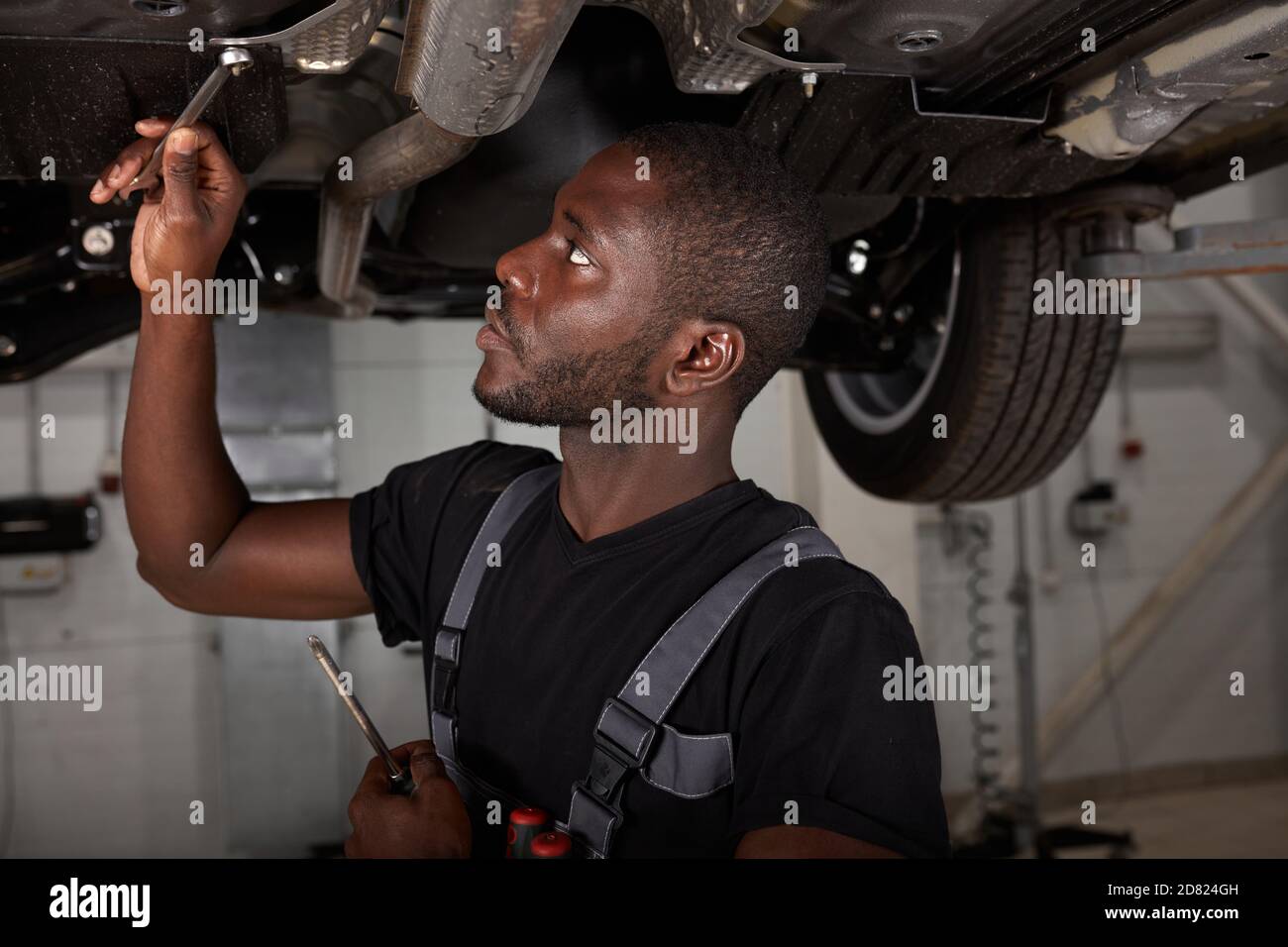 handsome african male repairing bottom of car, check and examine all ...
