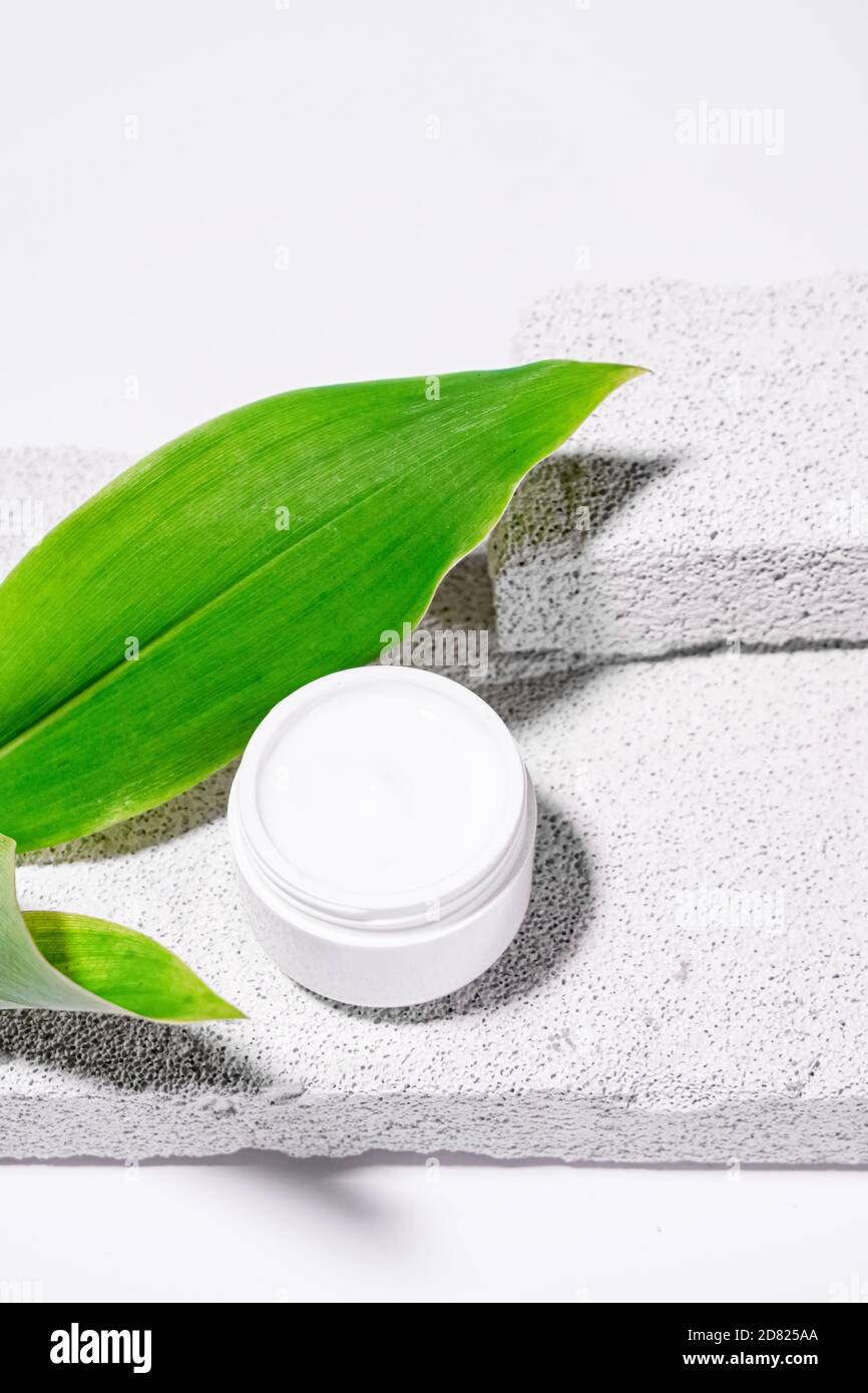 Cosmetic cream on natural white stone with green leaves on white bright ...