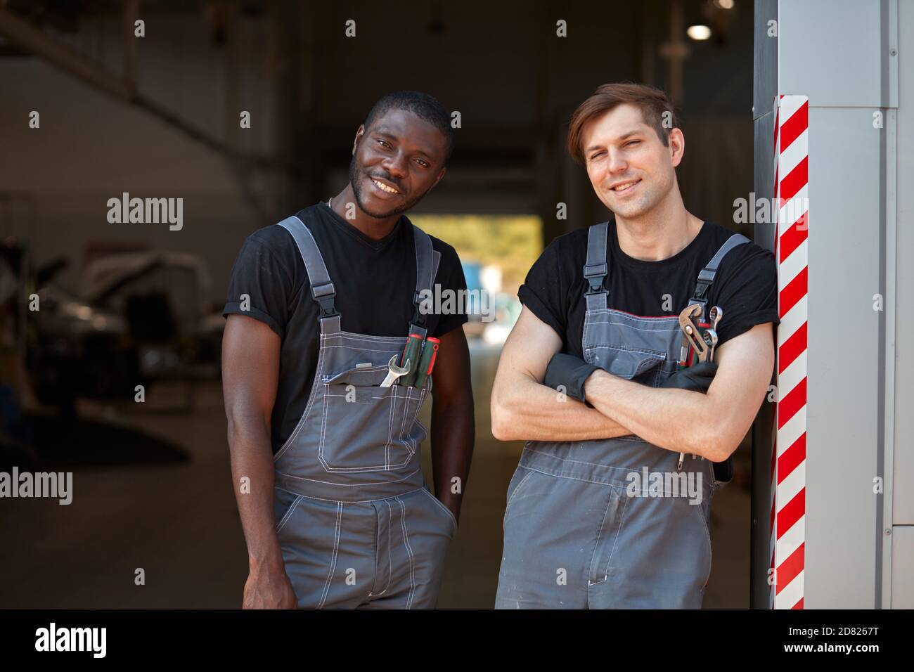 two diverse auto mechanic males have rest at work place, take a break ...