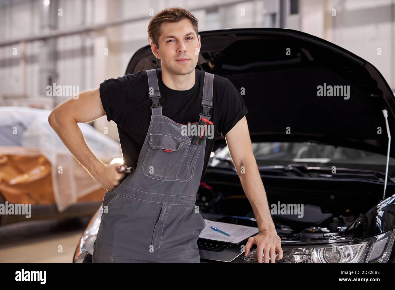 portrait of handsome caucasian auto mechanic man, standing near the car ...
