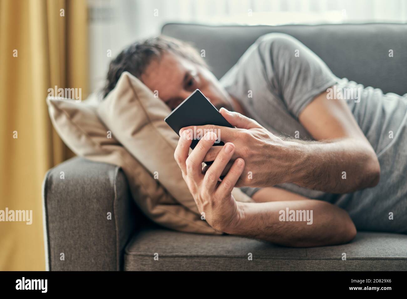 Depressed man using mobile phone while lying at living room sofa, adult ...