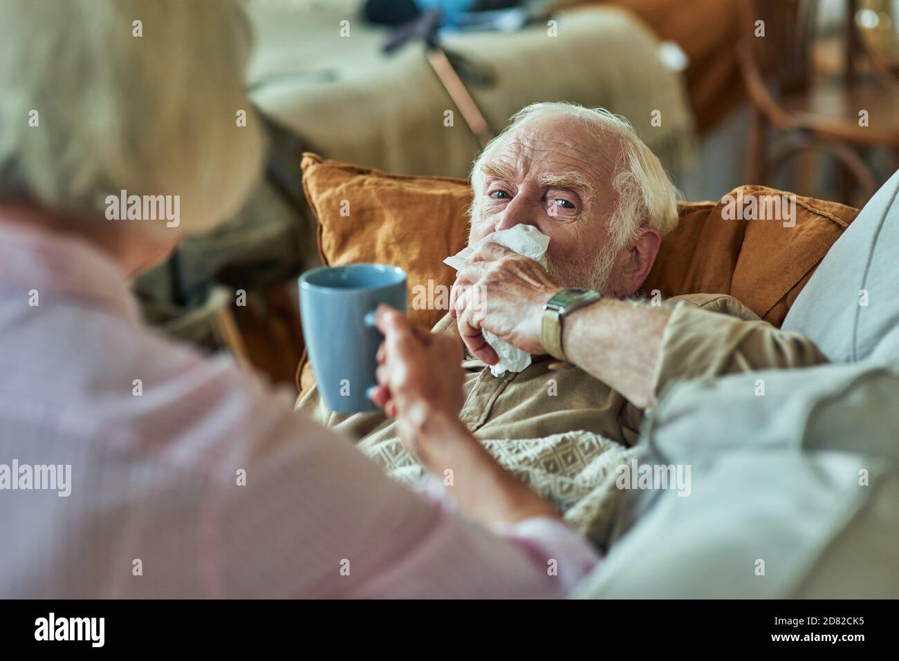 Sick elderly man lying on the couch and using his napkin for a runny ...