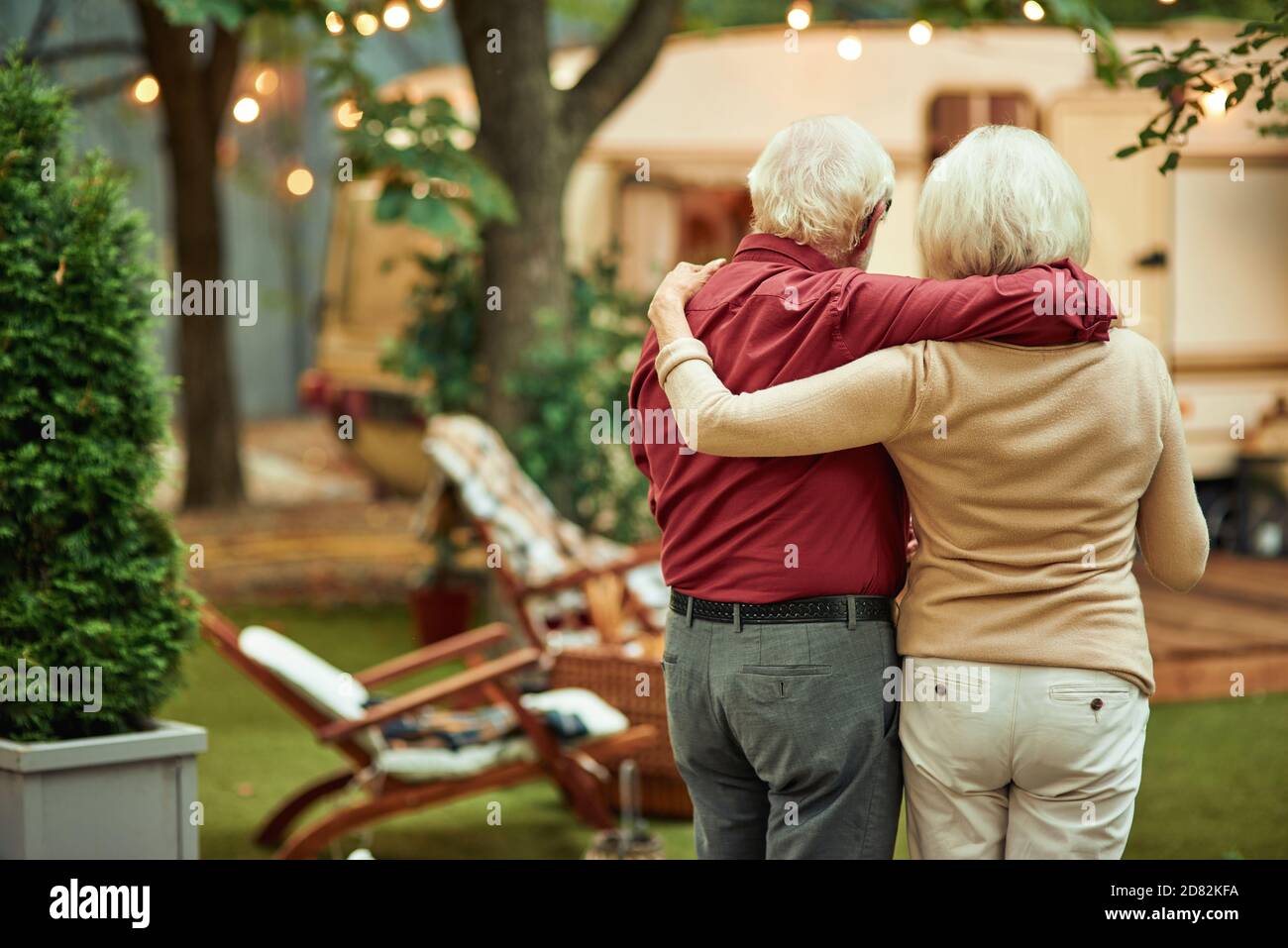 Back view of elderly couple hugging outdoors with their motorhome on ...