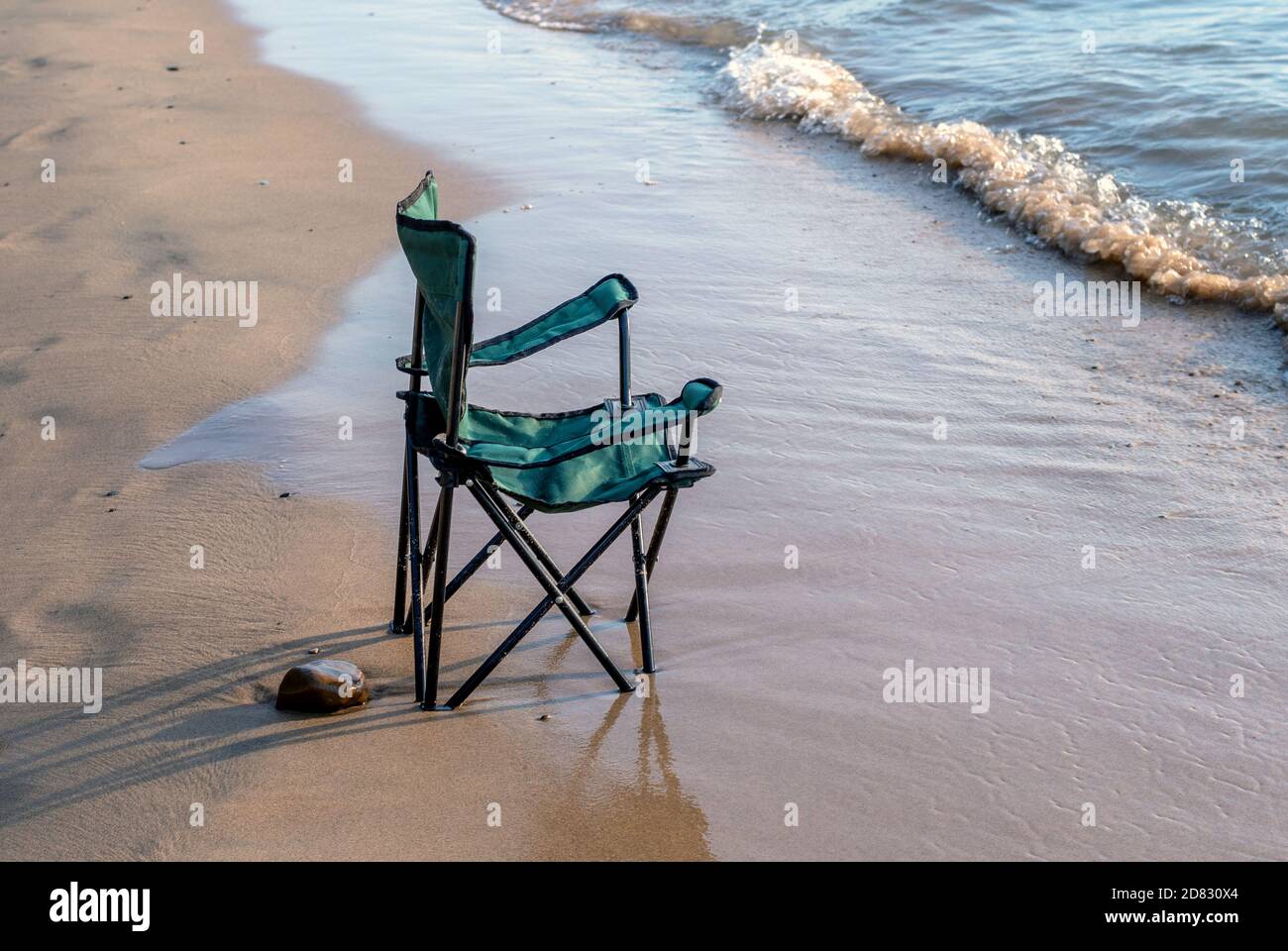 An cloth folding beach chair sits in the wet sand along the shores of ...