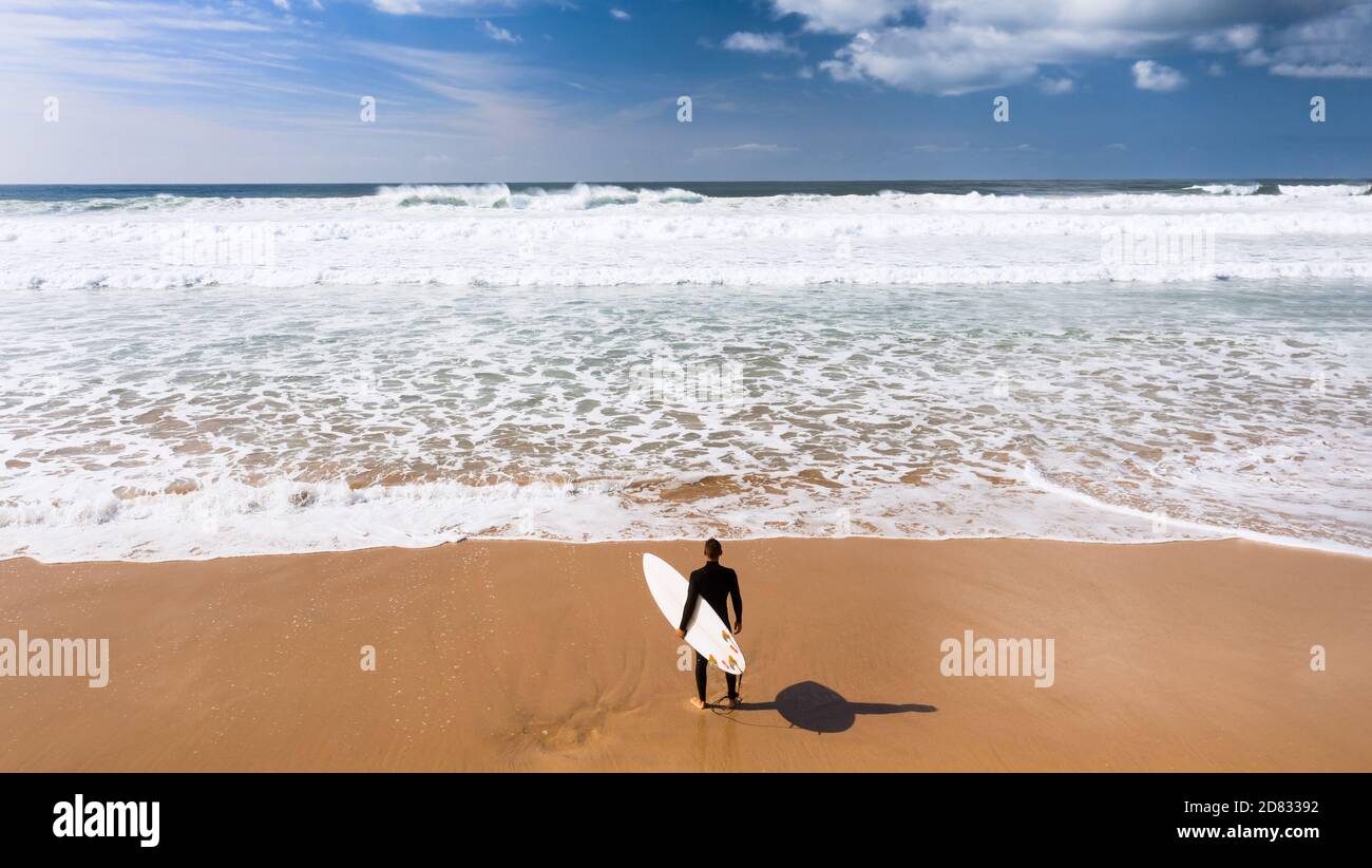 Top view of a man surfer in wetsuit with a surfboard standing near the ...