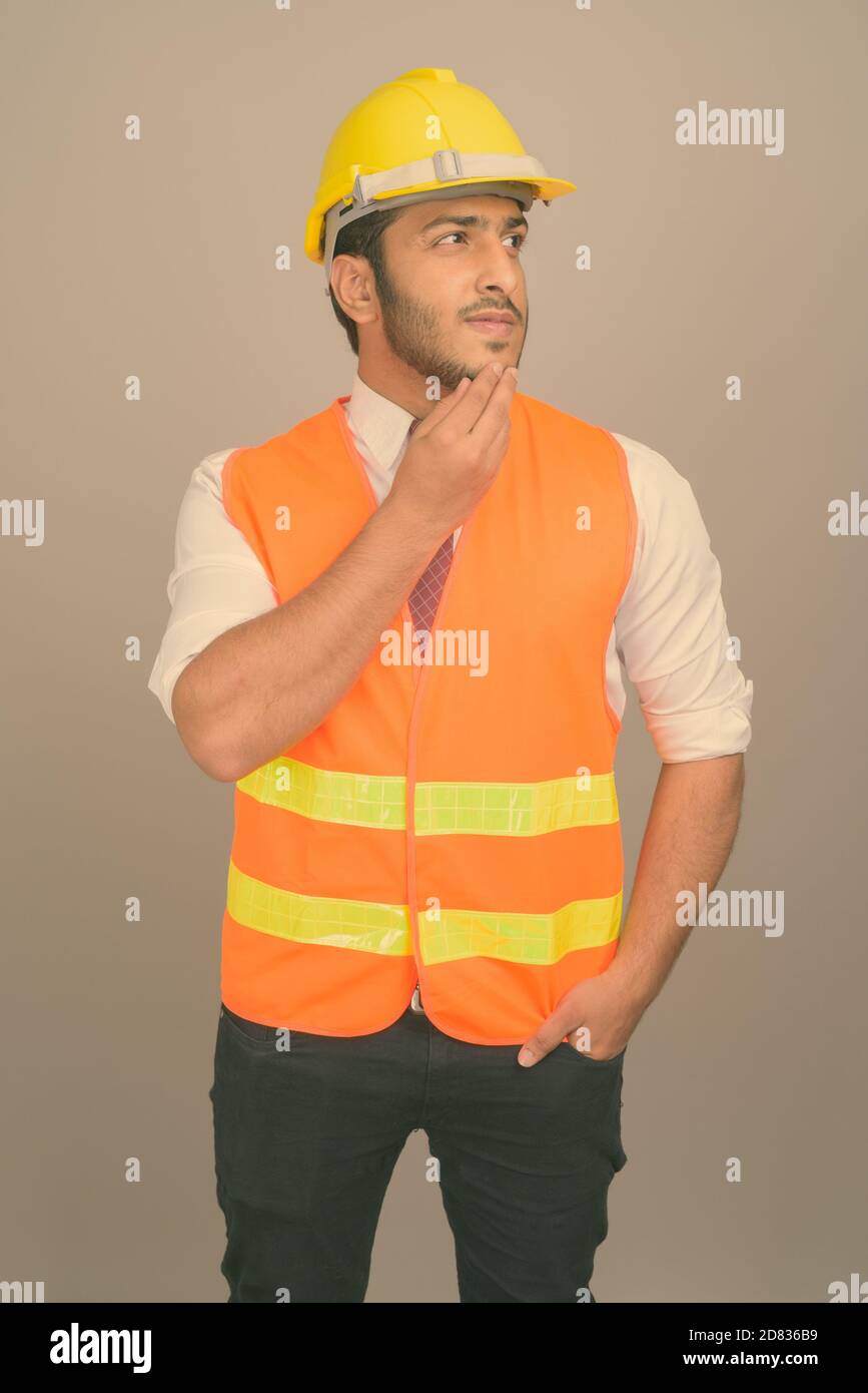 Young handsome Indian man construction worker against gray background ...