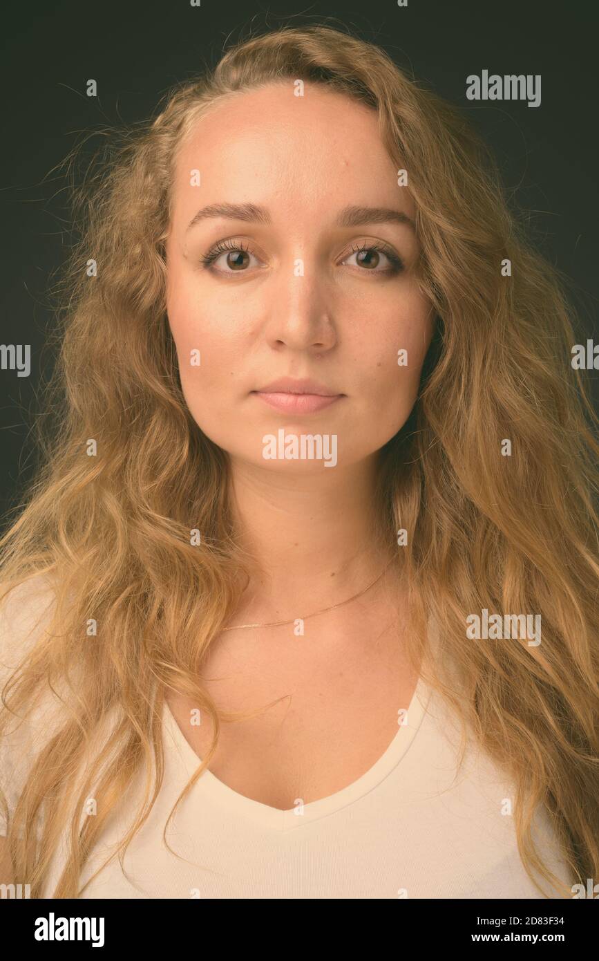 Young beautiful woman with long wavy blond hair against gray background ...
